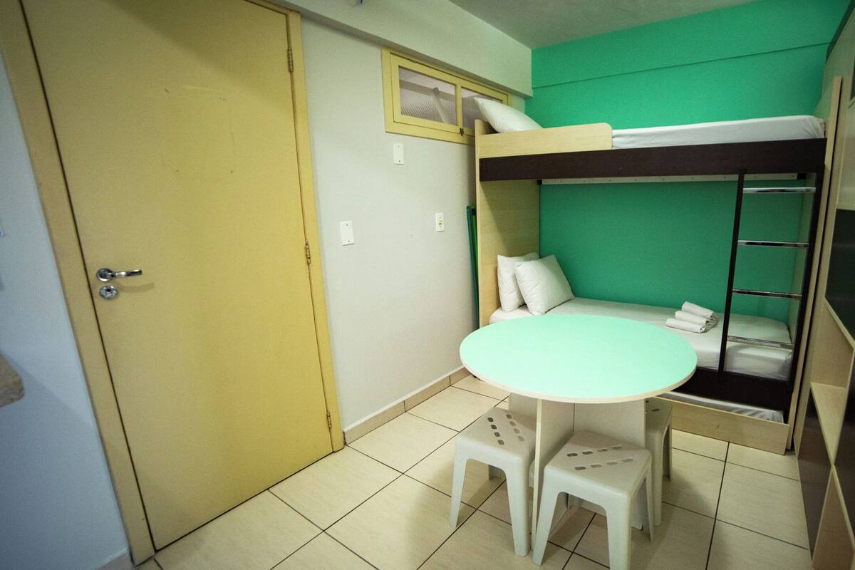 Quarto compacto com beliches, uma mesinha redonda e dois banquinhos.