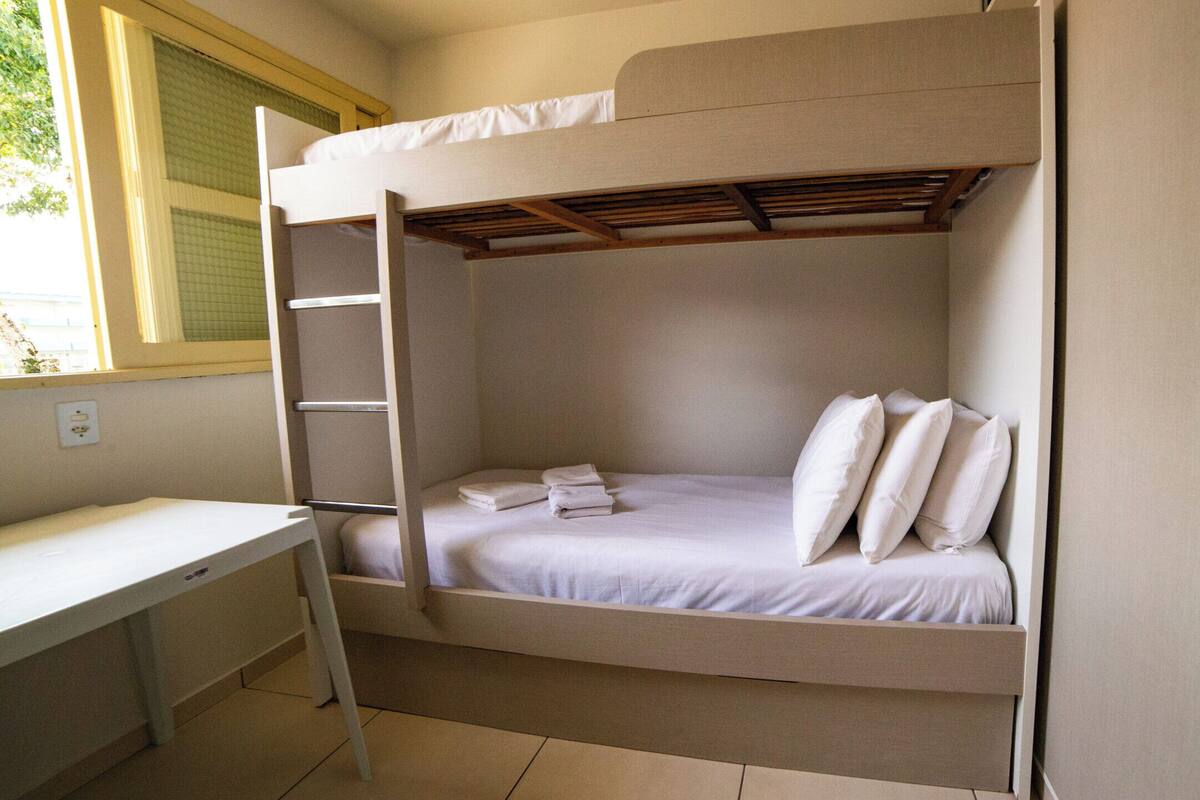 Uma cama beliche com escrivaninha e janela.
