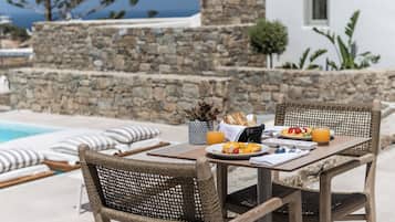 Uma mesa de jantar com cadeiras de vime, uma parede de pedra e vista para o mar.
