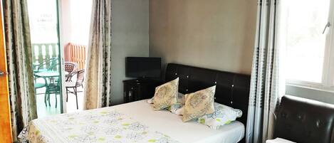 Quarto com cama, televisão, cadeira e varanda com mesa e cadeiras.