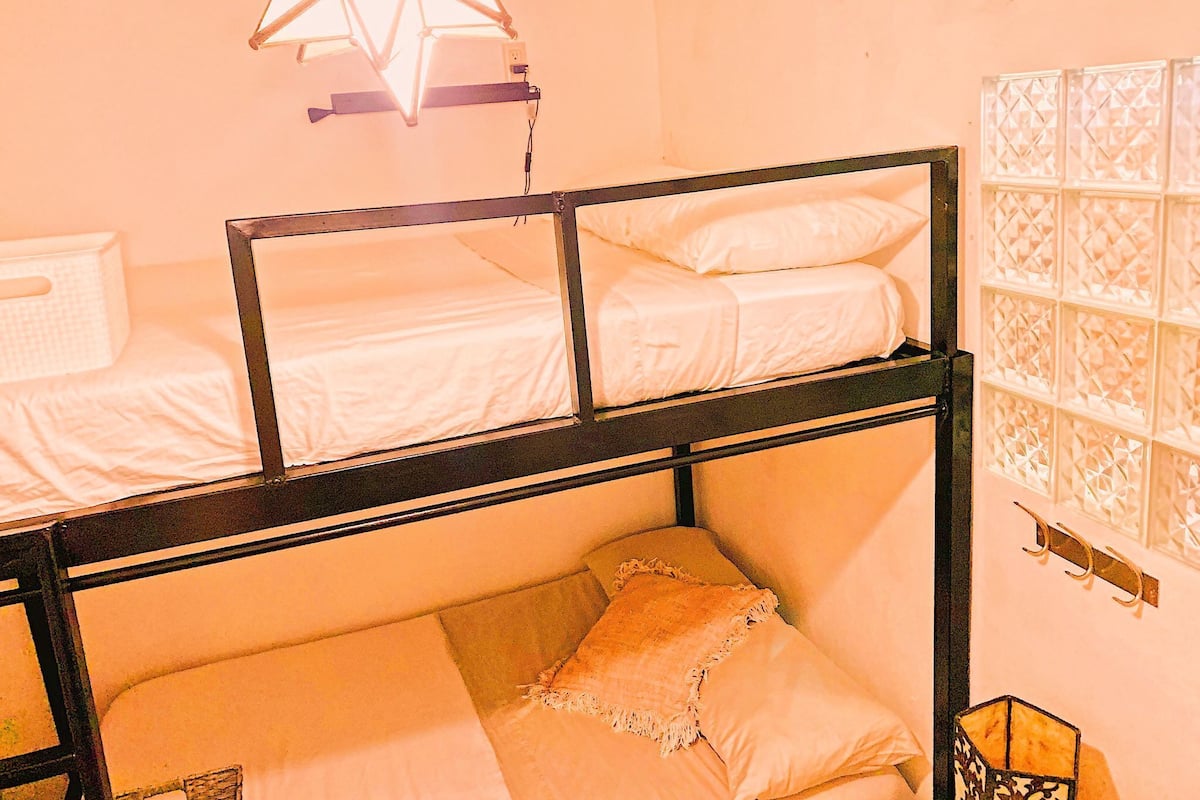 Uma cama beliche com um candeeiro em formato de estrela acima e uma persiana estampada ao lado direito.