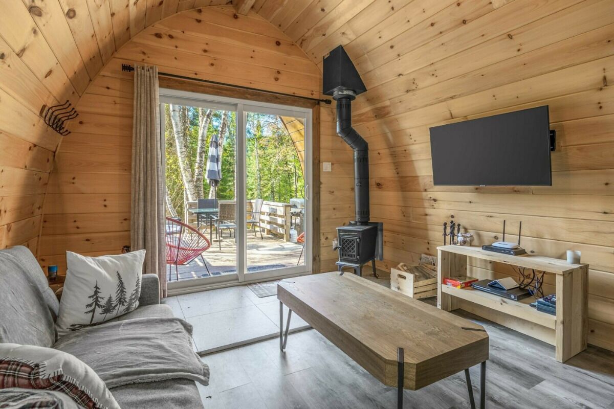 Interior acolhedor de uma cabana, com teto de madeira, sofá com almofada de design de árvore, um banco, TV na parede e lareira.