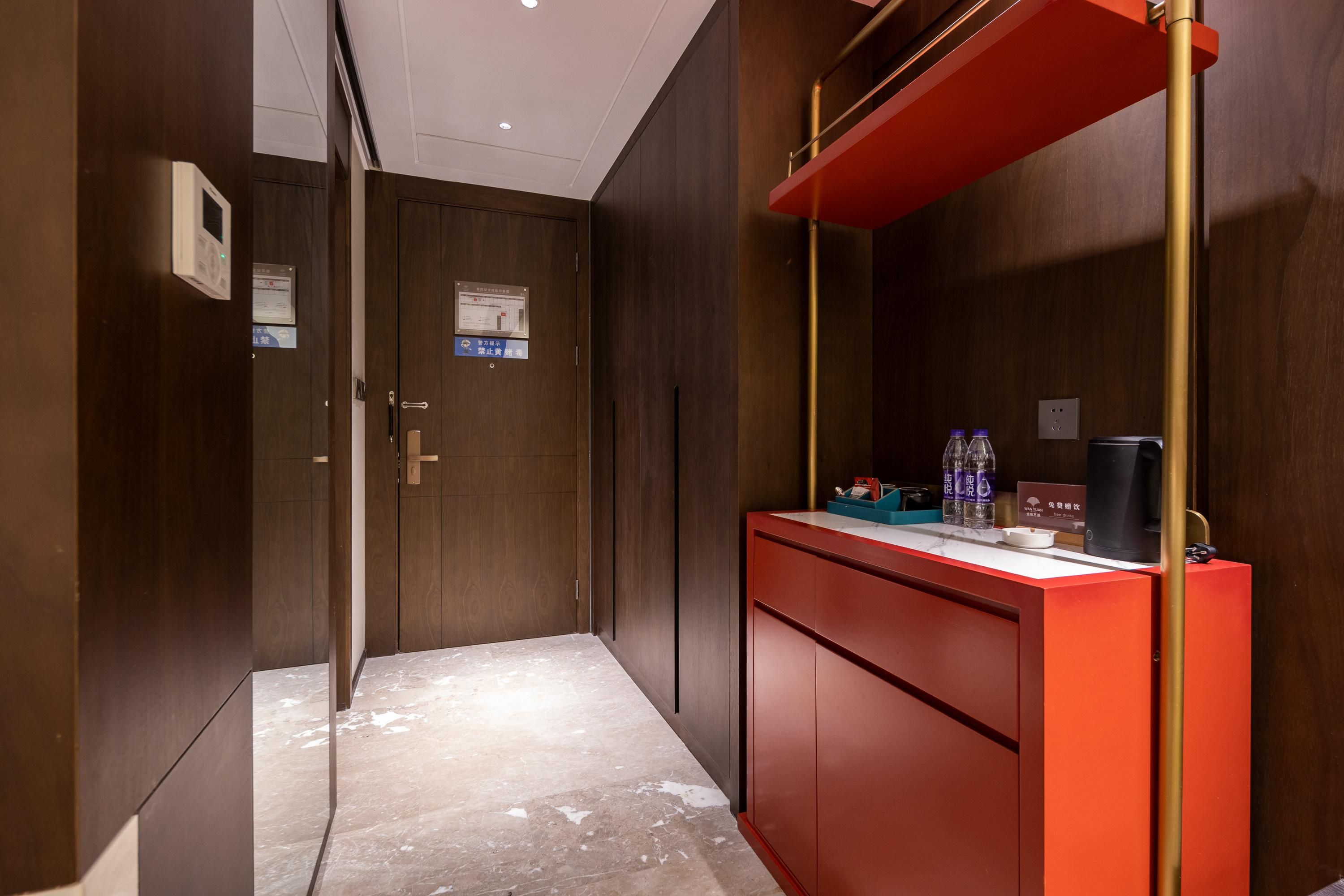 Um corredor com uma porta de madeira, um balcão vermelho com pia e um espelho.