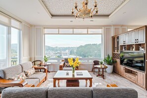 Uma sala de estar ampla com uma grande janela, um candelabro e uma televisão.