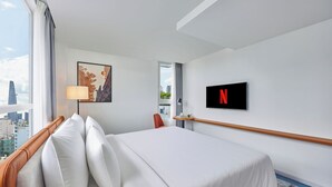 Quarto de hotel com uma cama grande, televisão na parede, vista para a cidade e janela com cortinas.