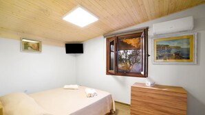 Quarto com cama, cómoda de madeira, televisão na parede e janela com persiana aberta.