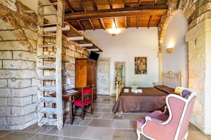 Quarto rústico com escada de madeira, uma mesa, uma cadeira, uma cama e uma parede de pedra.