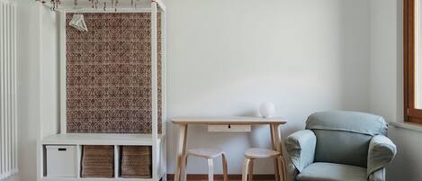 Quarto com guarda-roupa branco, uma pequena escrivaninha, duas cadeiras e uma janela.