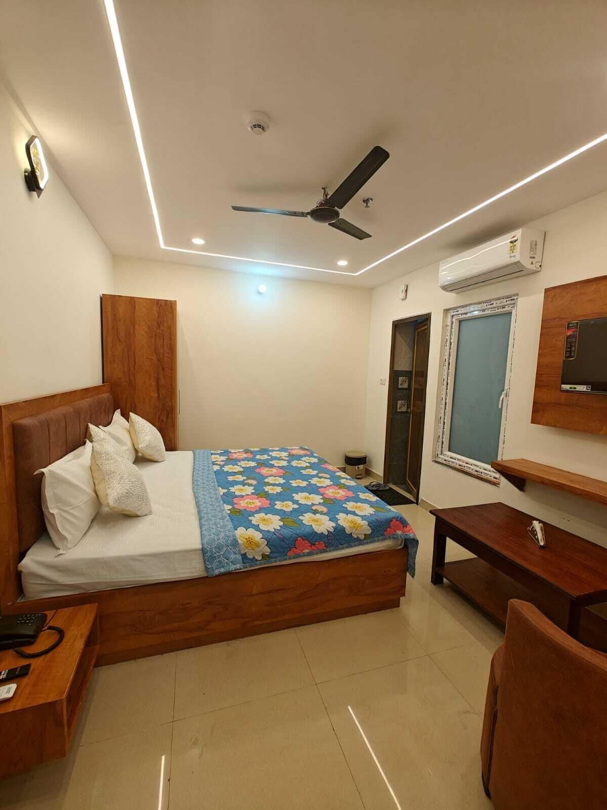 Quarto com cama de madeira, ventilador de teto, ar-condicionado, televisão e mesa de cabeceira.