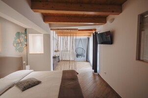 Quarto com cama, um banquinho, cadeira suspensa e televisão na parede.
