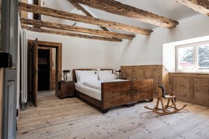 Quarto com cama de madeira, uma cadeira de balanço e vigas de madeira aparente.