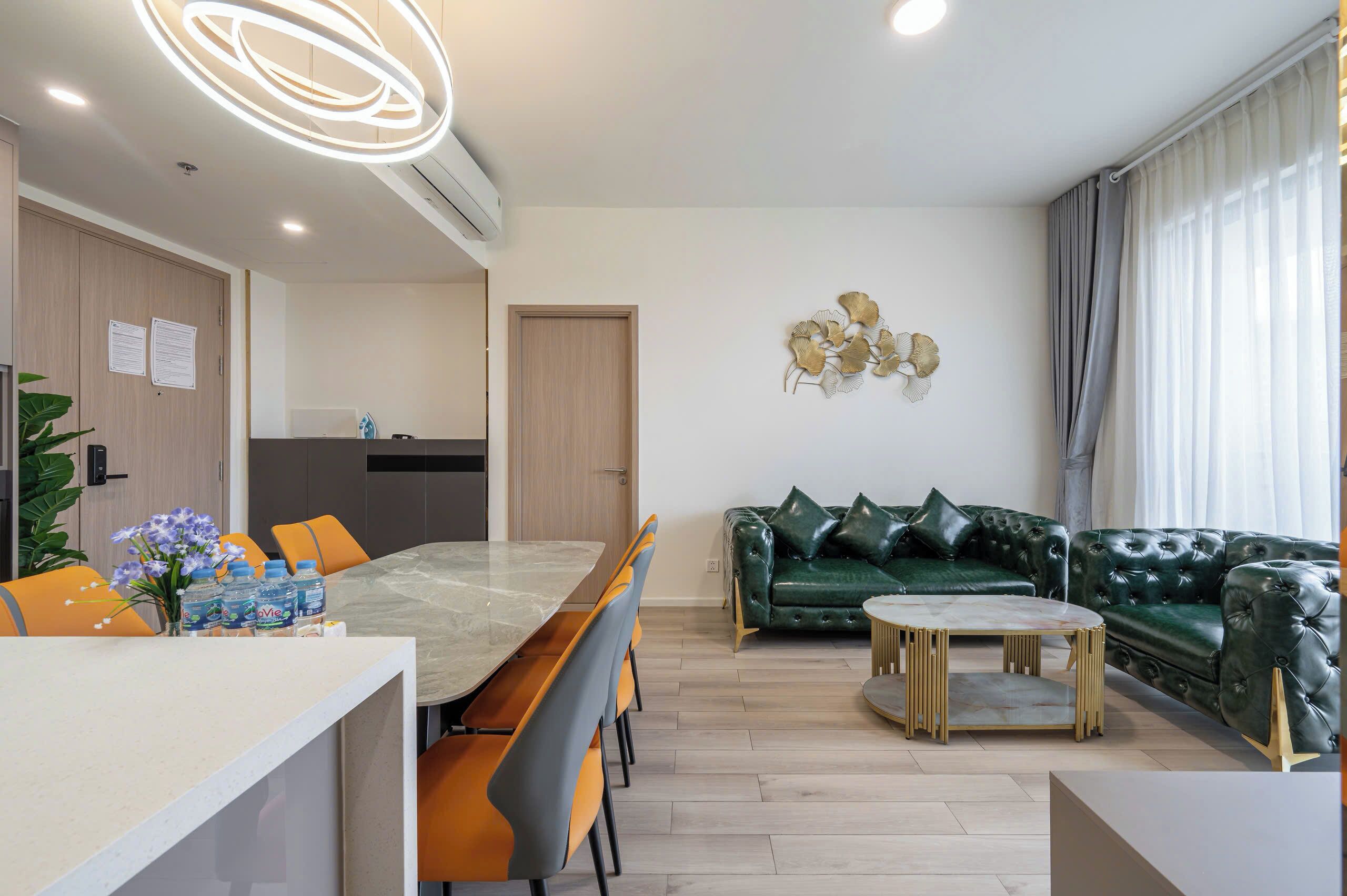 Uma sala de estar moderna com sofá de couro verde, uma mesa de jantar com cadeiras e um objeto decorativo na parede.