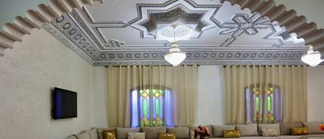 Uma sala de estar com sofá, banquinho, mesa de centro e lustre.
