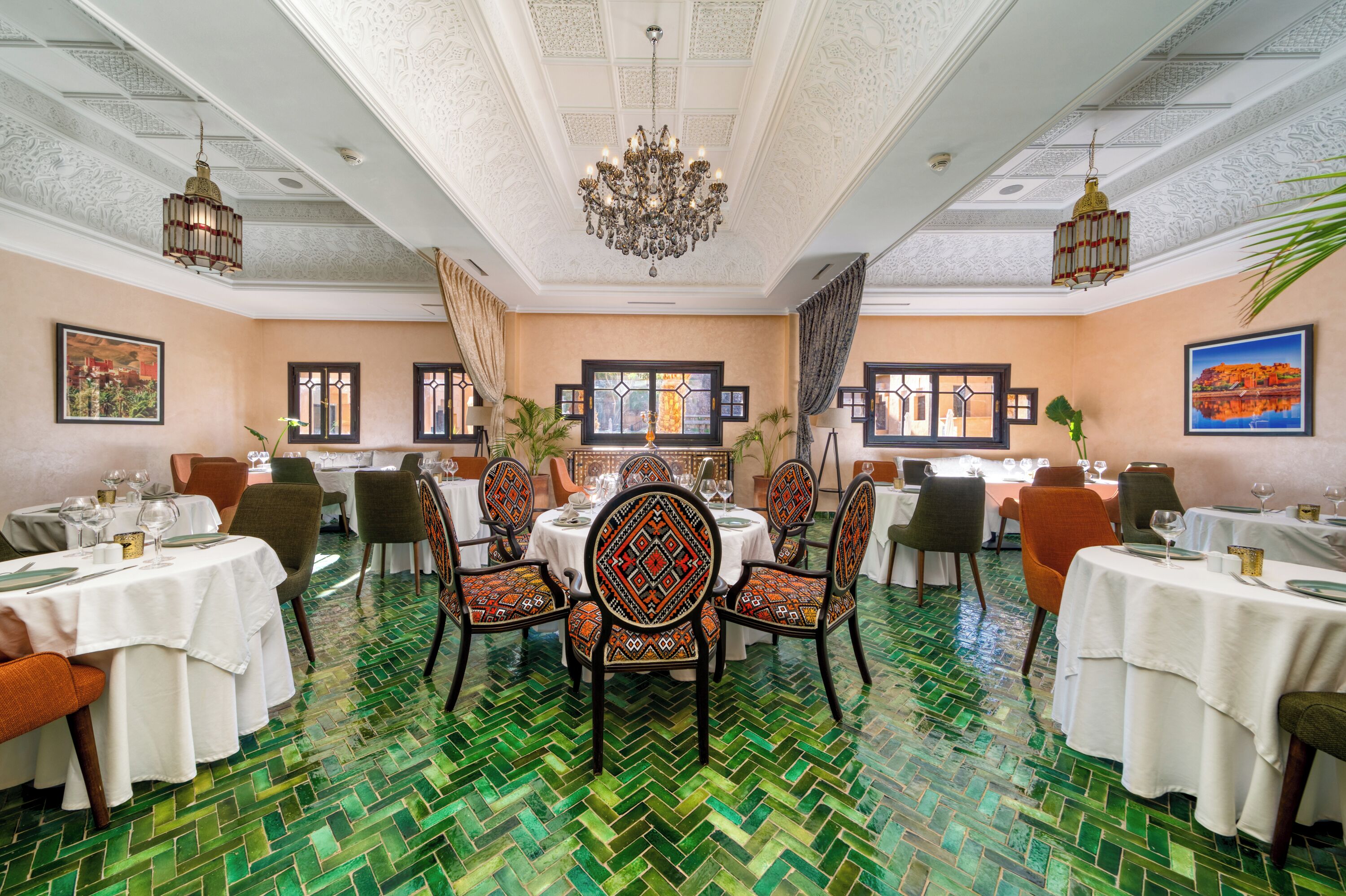 Uma sala de jantar com ladrilhos estampados, mesas redondas com toalhas brancas e cadeiras com estofamento padronizado.