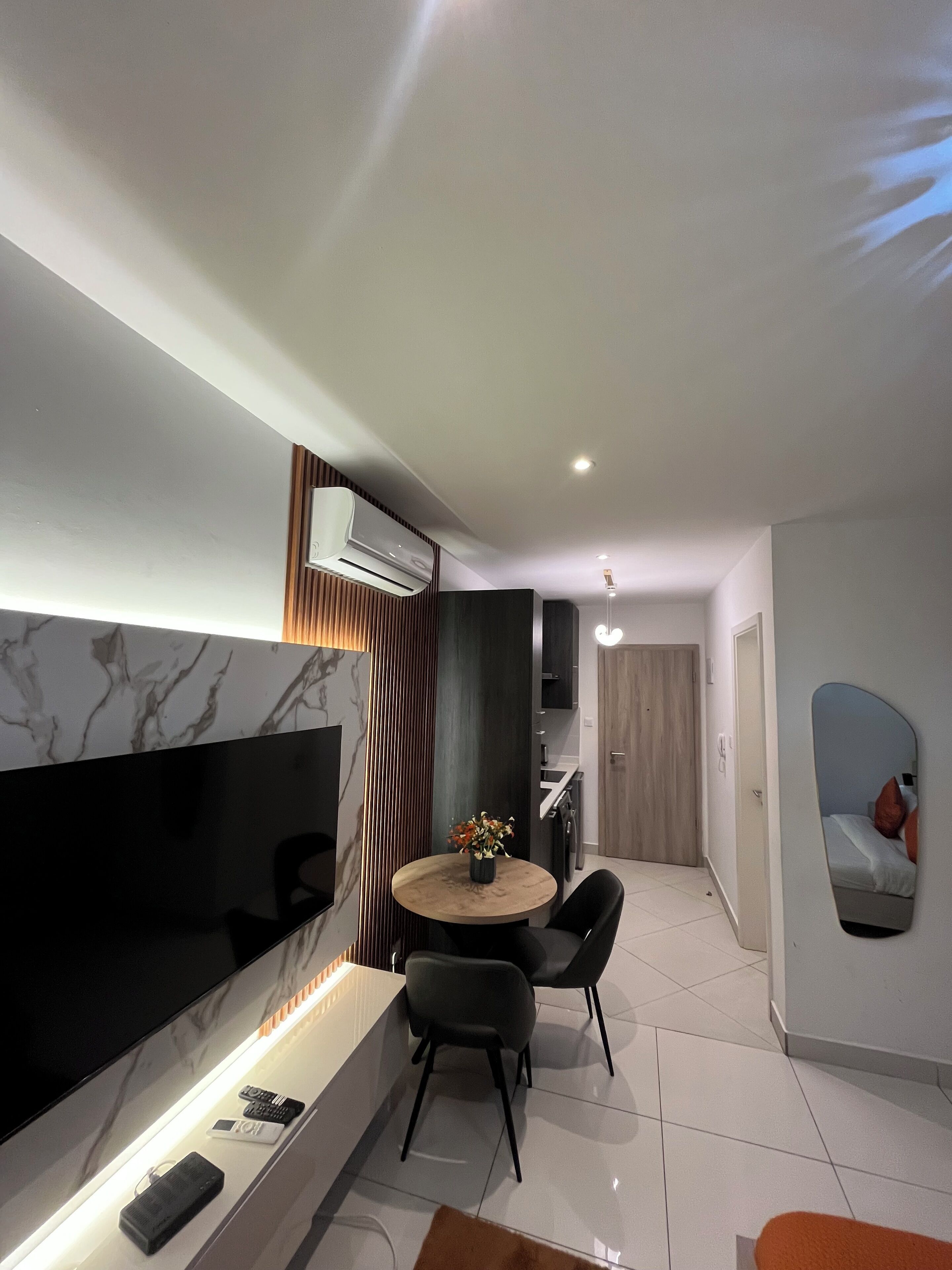 Uma sala de estar moderna com televisão de tela plana, uma mesa de madeira redonda com cadeiras e um ar condicionado instalado.