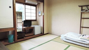Quarto japonês tradicional com tatames, televisão, pequeno frigorífico e futon.