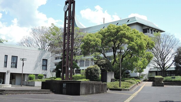 Um edifício com torre do relógio, rodeado por árvores e céu claro.