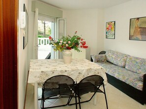 Uma área de refeições com uma mesa posta para dois, um vaso com flores e um sofá com almofadas estampadas.