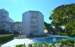 Um edifício com vários andares, varandas, piscina e vegetação ao redor.