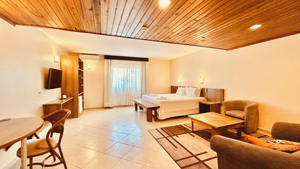 Quarto de hotel com teto de madeira, cama, escrivaninha, cadeira, sofá e televisão.