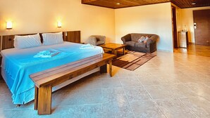 Quarto de hotel moderno com uma cama grande, um banco de madeira, um sofá e uma mesa de centro.