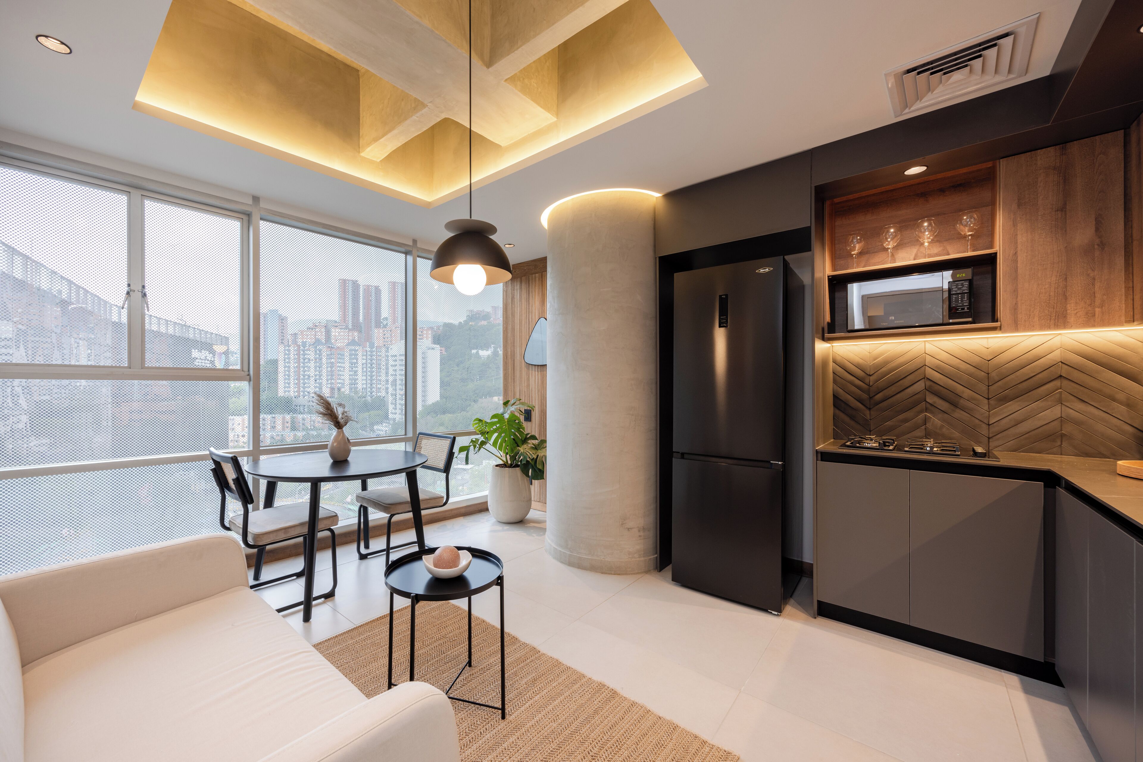 Uma cozinha moderna com micro-ondas e frigorífico embutidos, zona de refeições com mesa e cadeiras, e uma janela grande com vista para a cidade.