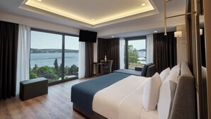 Quarto de hotel moderno com uma cama grande, uma escrivaninha e vista para a água.