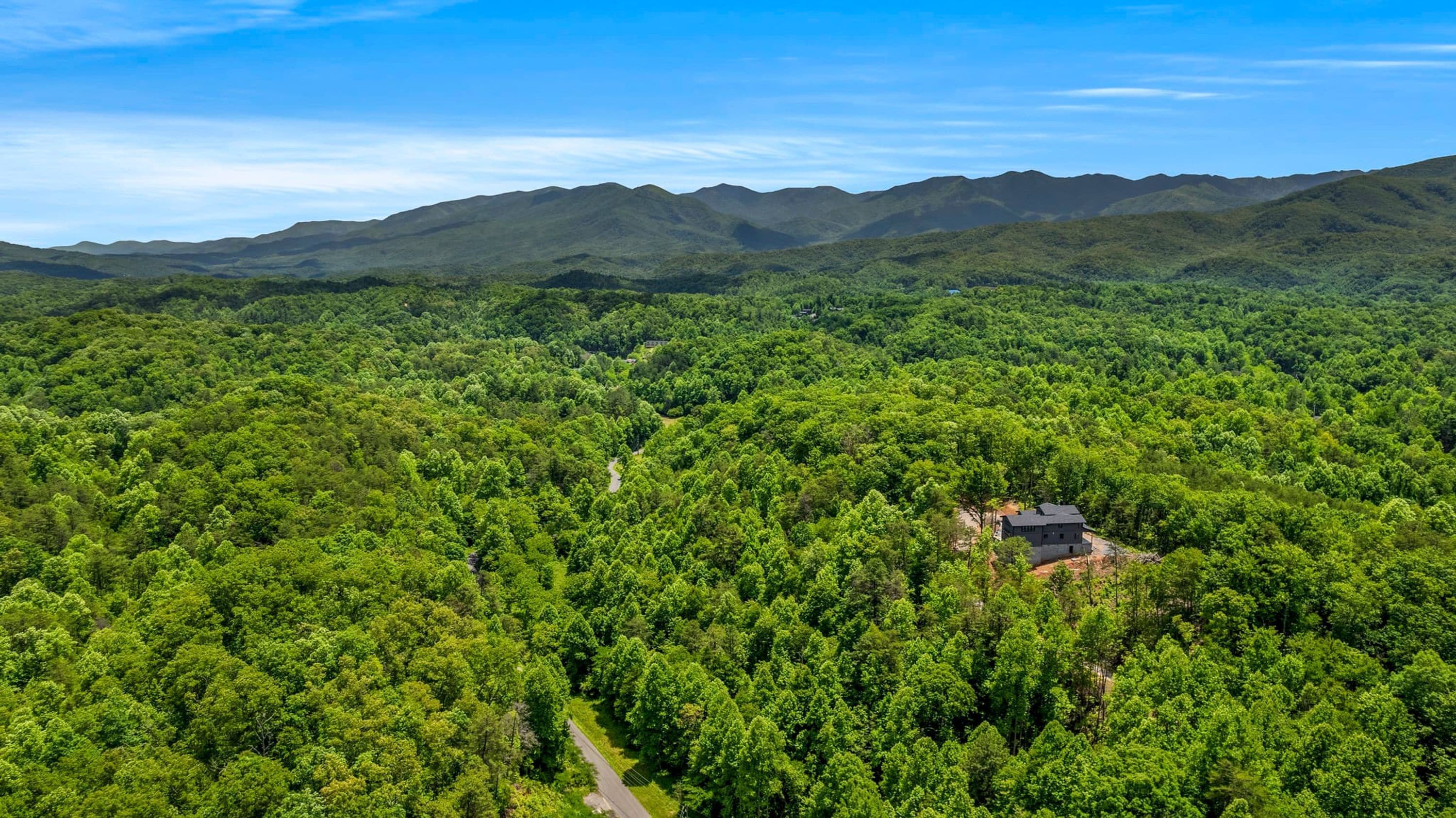 Uma área arborizada com um pequeno edifício rodeado por árvores densas e colinas ao fundo.