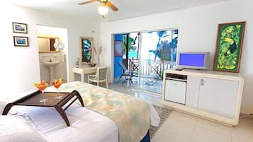 Quarto de hotel com cama, escrivaninha, televisão, varanda com vista e ventoinha.