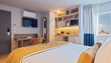 Quarto de hotel com cama, escrivaninha, televisão, espelho e janela com cortinas.