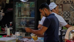 Uma cozinha com panelas e frigideiras penduradas, uma geladeira e um balcão com alimentos.