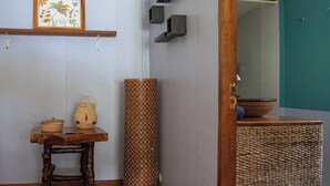 Um quarto com uma mesa de madeira, uma cesta trançada, um objeto cilíndrico tecido e um quadro na parede.