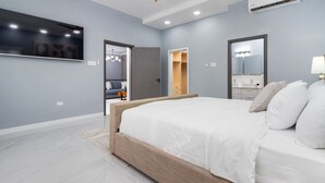 Quarto moderno com uma cama grande, ventoinha no teto, aparelho de ar condicionado, TV montada na parede e um closet espaçoso.