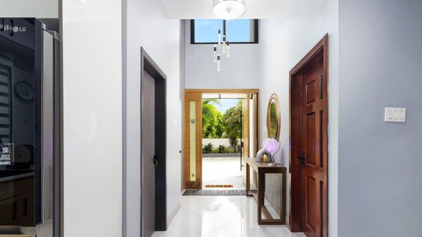 Um corredor com área de cozinha moderna, porta de madeira e vista para um jardim.