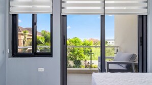 Quarto com uma cama, varanda com uma cadeira e vista para vegetação e edifícios.