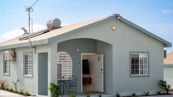 Uma casa térrea com telhado inclinado, varanda coberta com mesa e cadeiras, e antena parabólica no telhado.