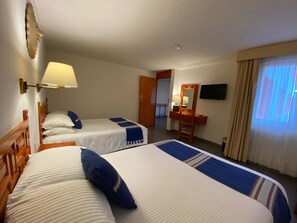 Quarto de hotel com duas camas, uma escrivaninha, um espelho e uma televisão.