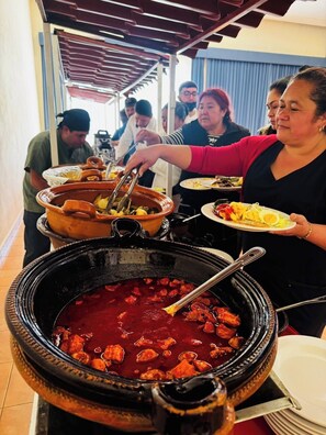 Uma área de refeições compartilhada com grandes panelas de comida, piso de azulejos e teto de metal corrugado.