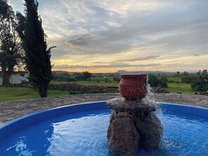 Uma fonte de pedra em uma piscina azul com vista para o pôr do sol.