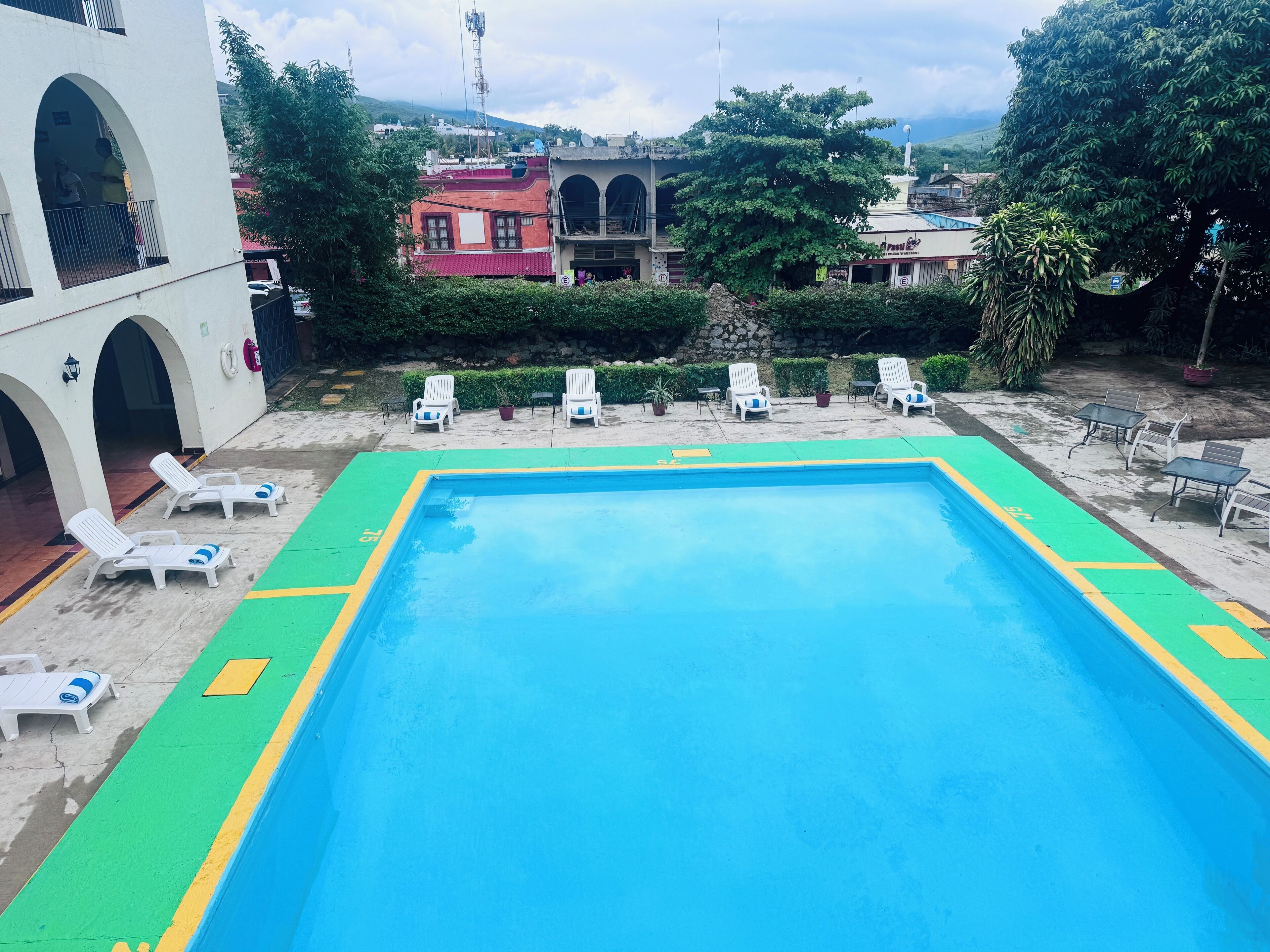 Piscina com espreguiçadeiras e um edifício com arcos ao fundo.