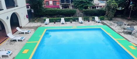 Piscina com espreguiçadeiras e um edifício com arcos ao fundo.