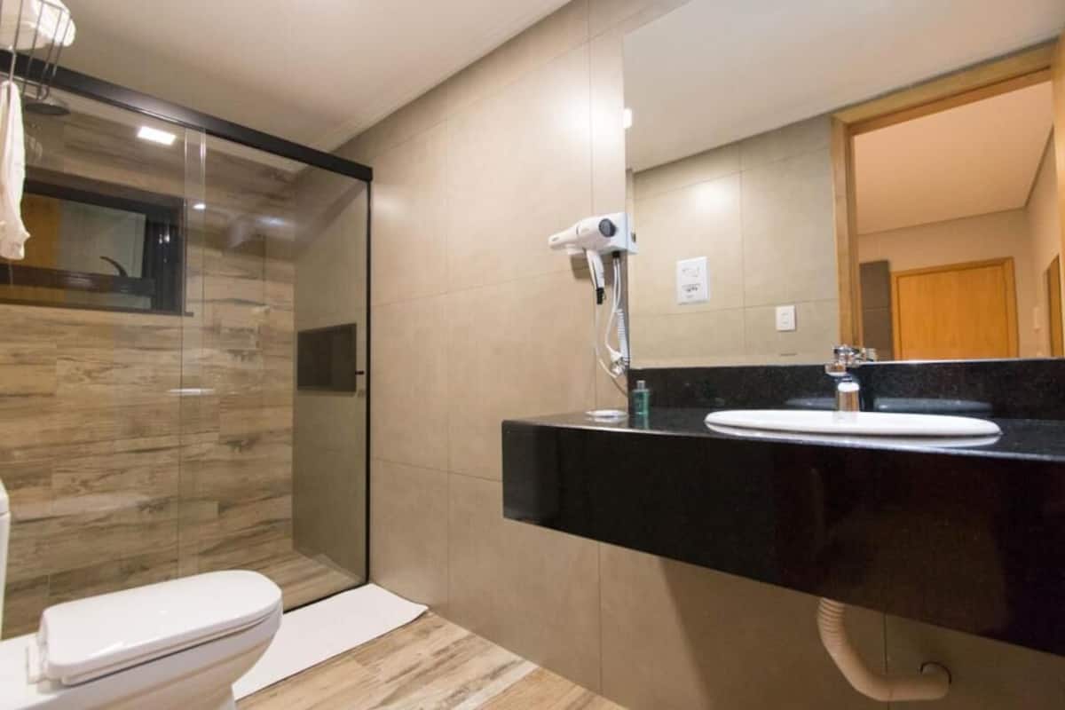 Casa de banho moderna com cabine de chuveiro em vidro, lavatório com bancada preta e espelho em cima.