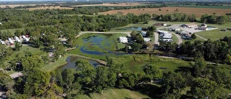 Vista aérea de um camping com trailers, um lago e vegetação ao redor.