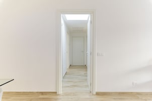 Um corredor com claraboia, paredes brancas e chão de madeira.