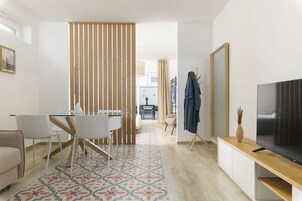 Uma sala de estar moderna com televisão, sofá, área de jantar com mesa e cadeiras, e um tapete estampado.