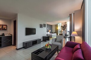 Uma sala de estar moderna com televisão de tela plana, um sofá, uma mesa de centro com frutas e uma área de jantar com luminária.