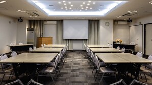 Uma sala de conferências com uma mesa comprida, cadeiras, tela de projetor e um relógio na parede.
