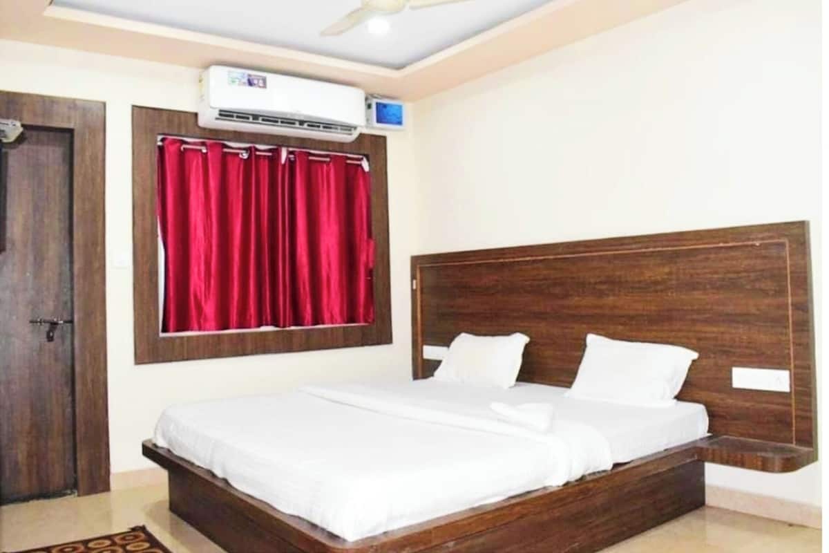 Quarto com cama de madeira, cortinas vermelhas, ar condicionado e ventoinha no teto.