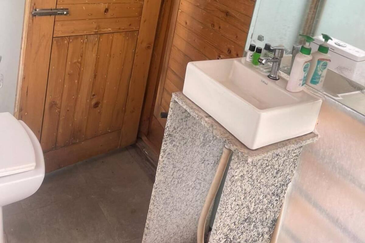Um banheiro com porta de madeira, pia branca com bancada de granito e espelho sobre a pia.