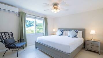 Quarto com cama, cadeira, mesa de cabeceira, ventoinha no teto e janela.
